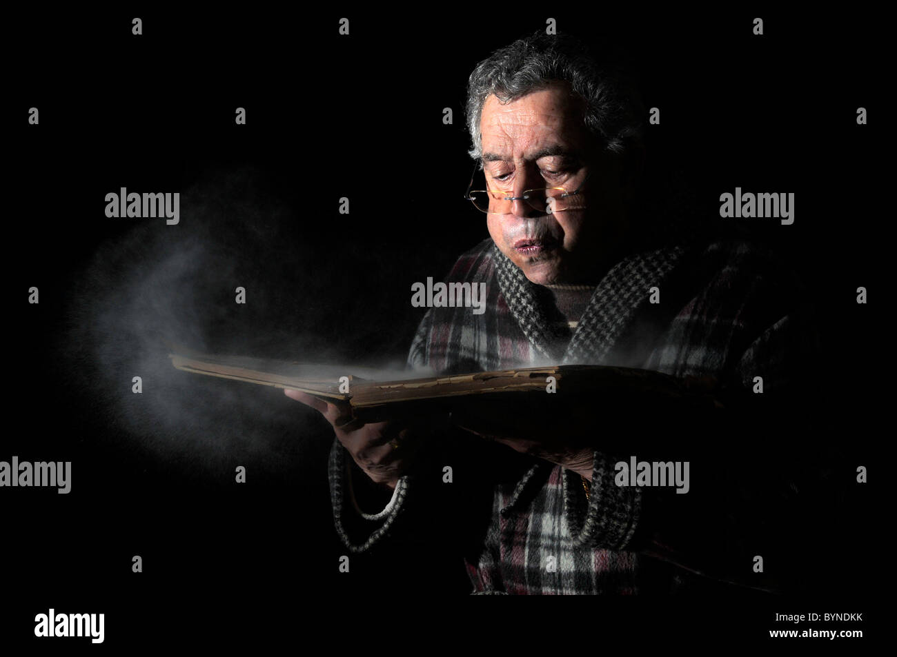 Senior man blowing dust of a very old book isolated in black Stock ...