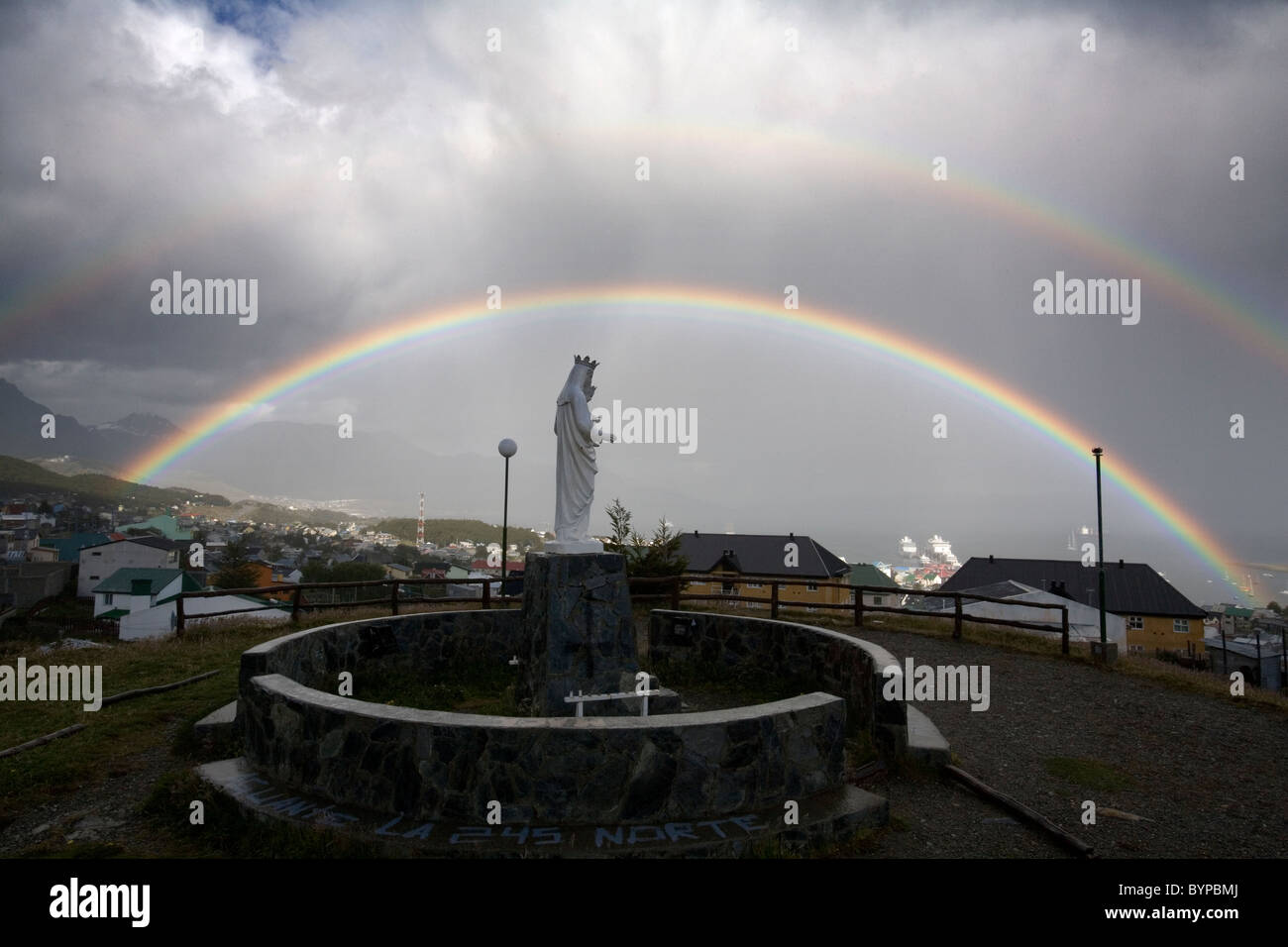 Statue of Virgin Mary under a large rainbow on top of the city of ...