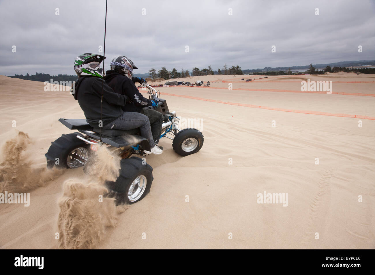 USA, Oregon, North Bend, Couple rides on ATV from high ridge of sand at ...