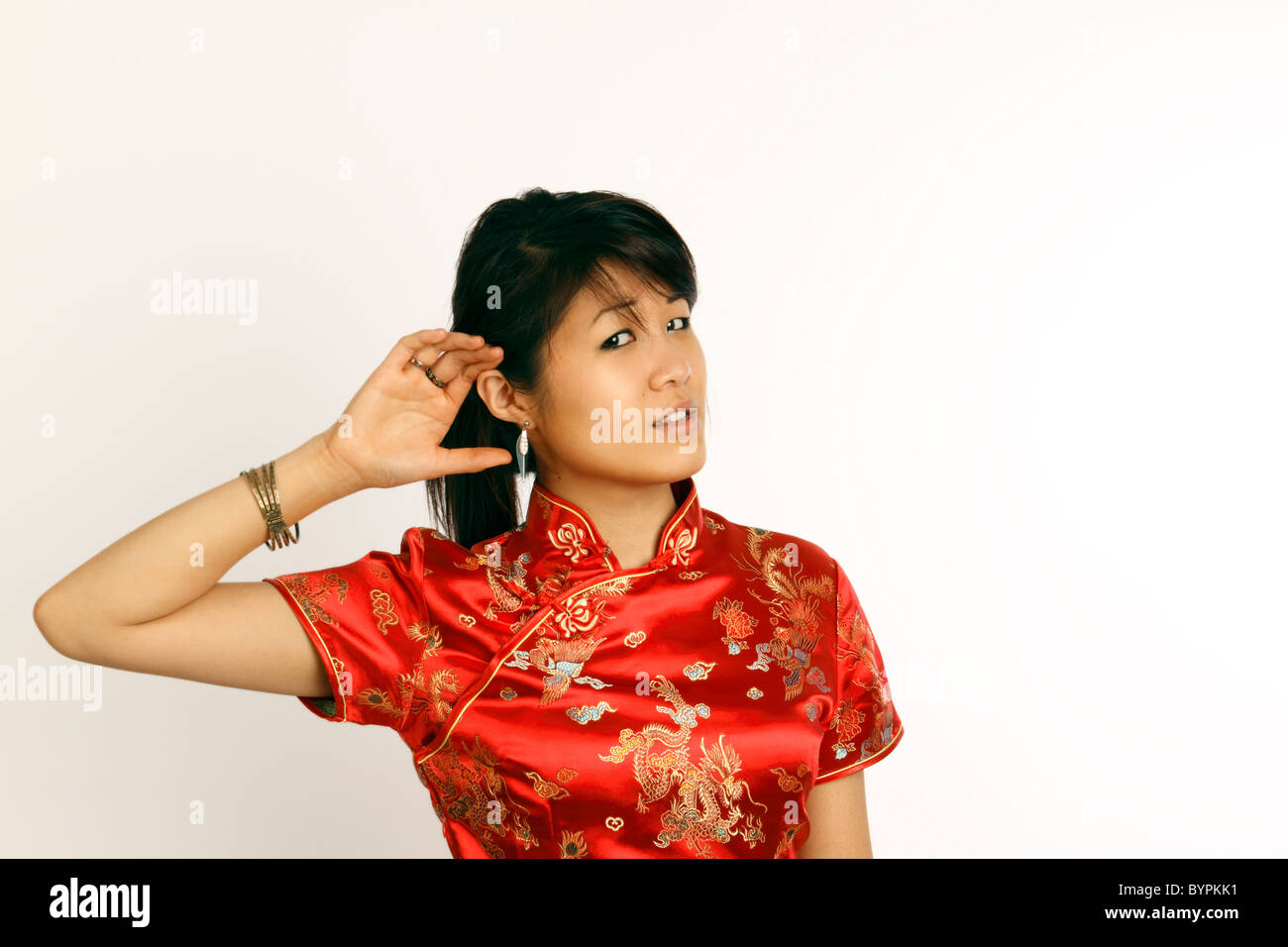 Young Chinese or oriental girl holding her hand to her ear to listen ...