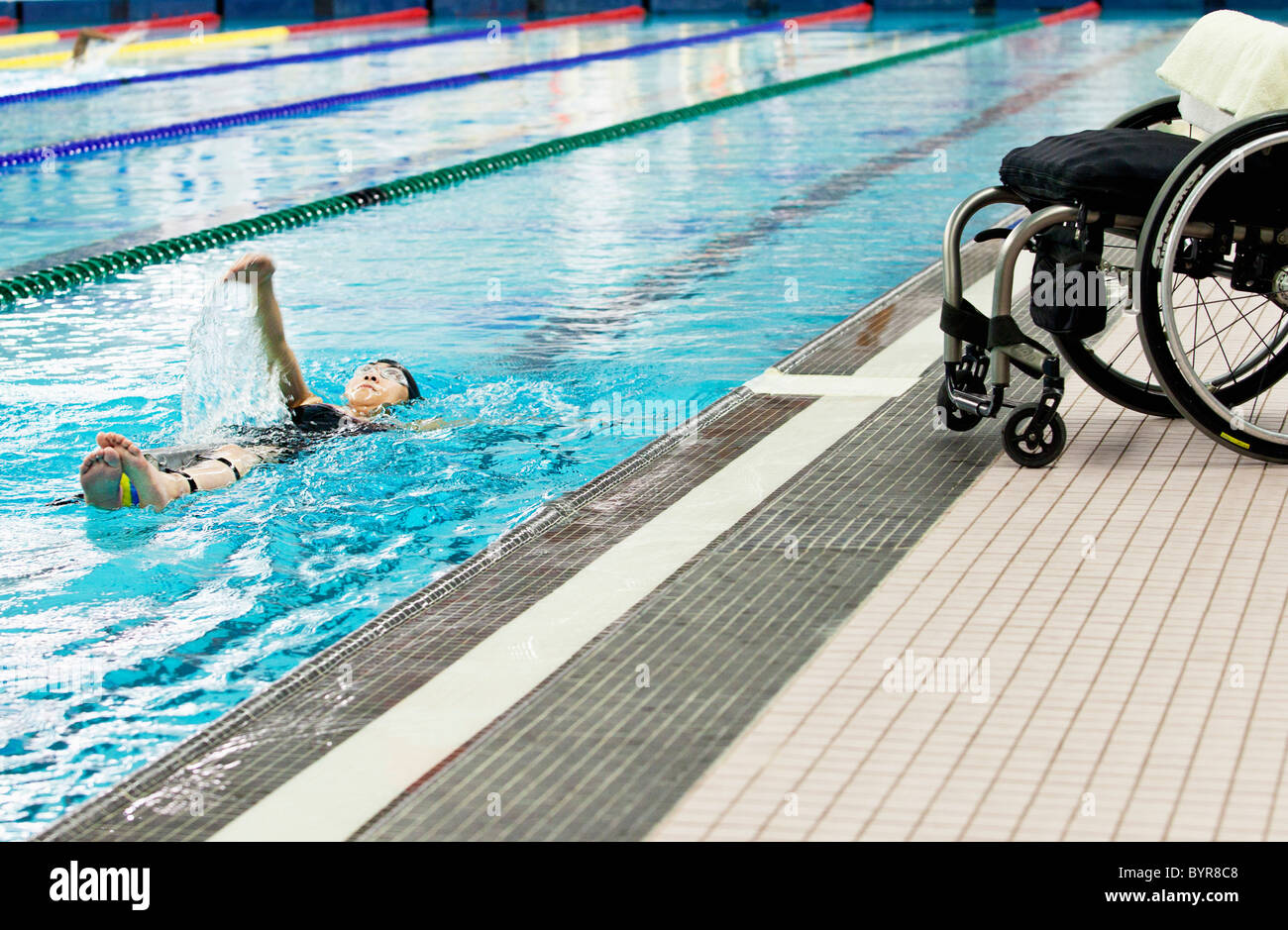 a paraplegic woman swims in a pool with her wheelchair at the edge of ...