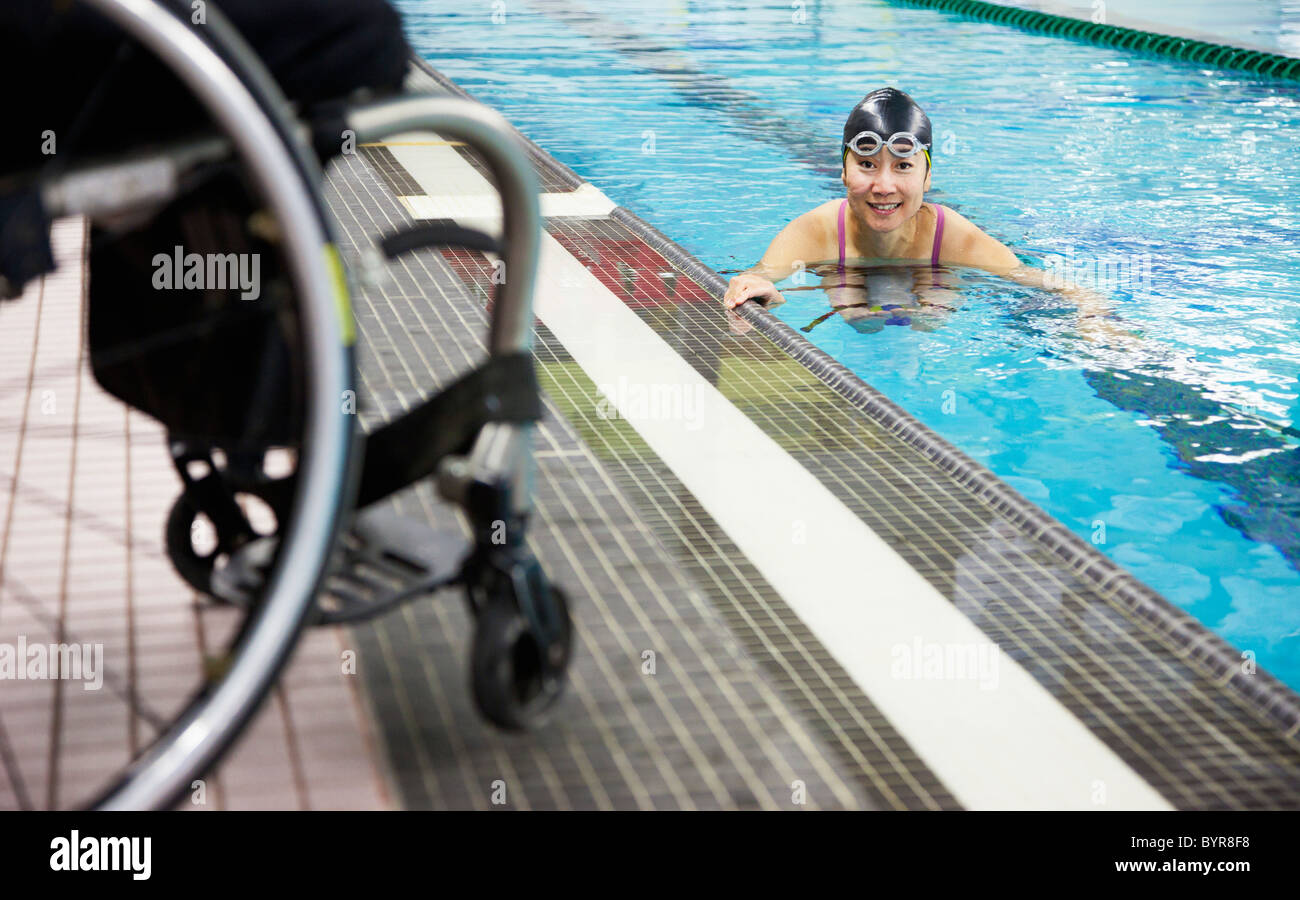a paraplegic woman swims in a pool with her wheelchair at the water's ...