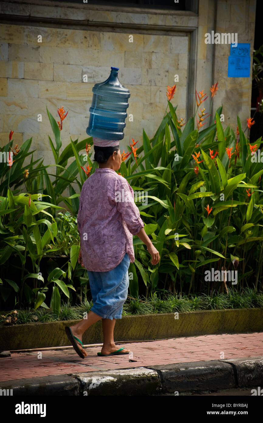 A Balinese woman walks down an Ubud, Bali, sidewalk while balancing a ...