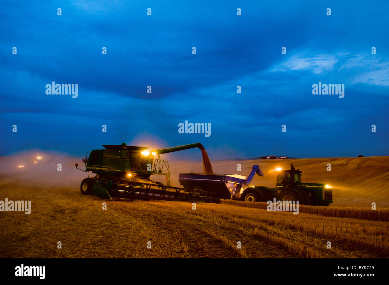 A John Deere combine harvests wheat while unloading to a grain cart “on ...