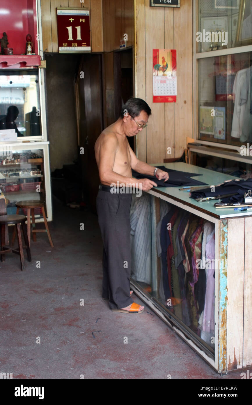 A bare chested Chinese tailor is working in a small custom shirt ...