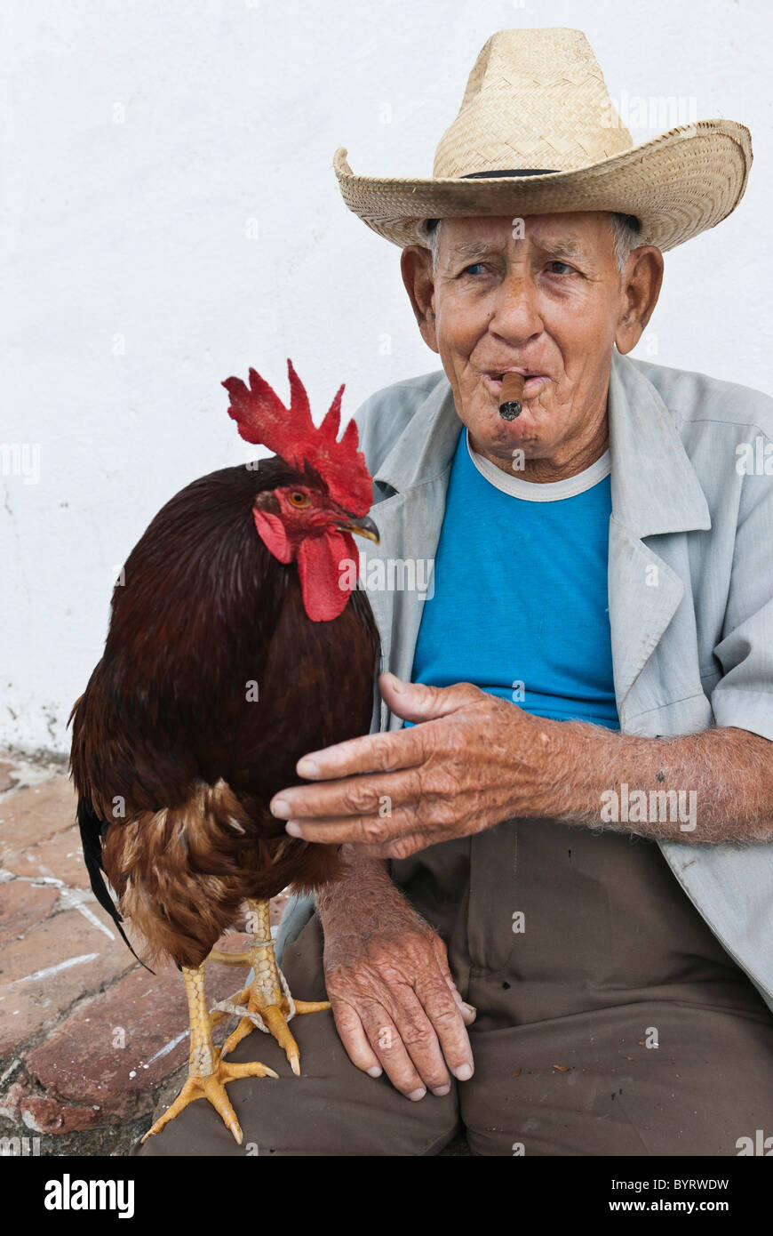 Old man with straw hat holding a rooster on his leg, Trinidad, Sancti ...