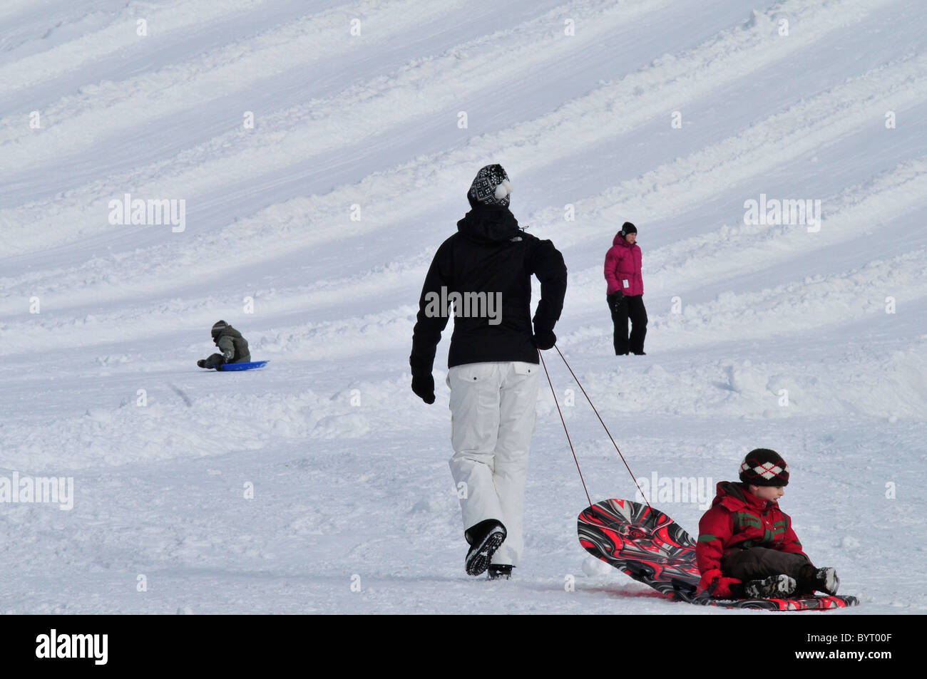 A woman drags her child up hill on a snowboard to glide down part of ...