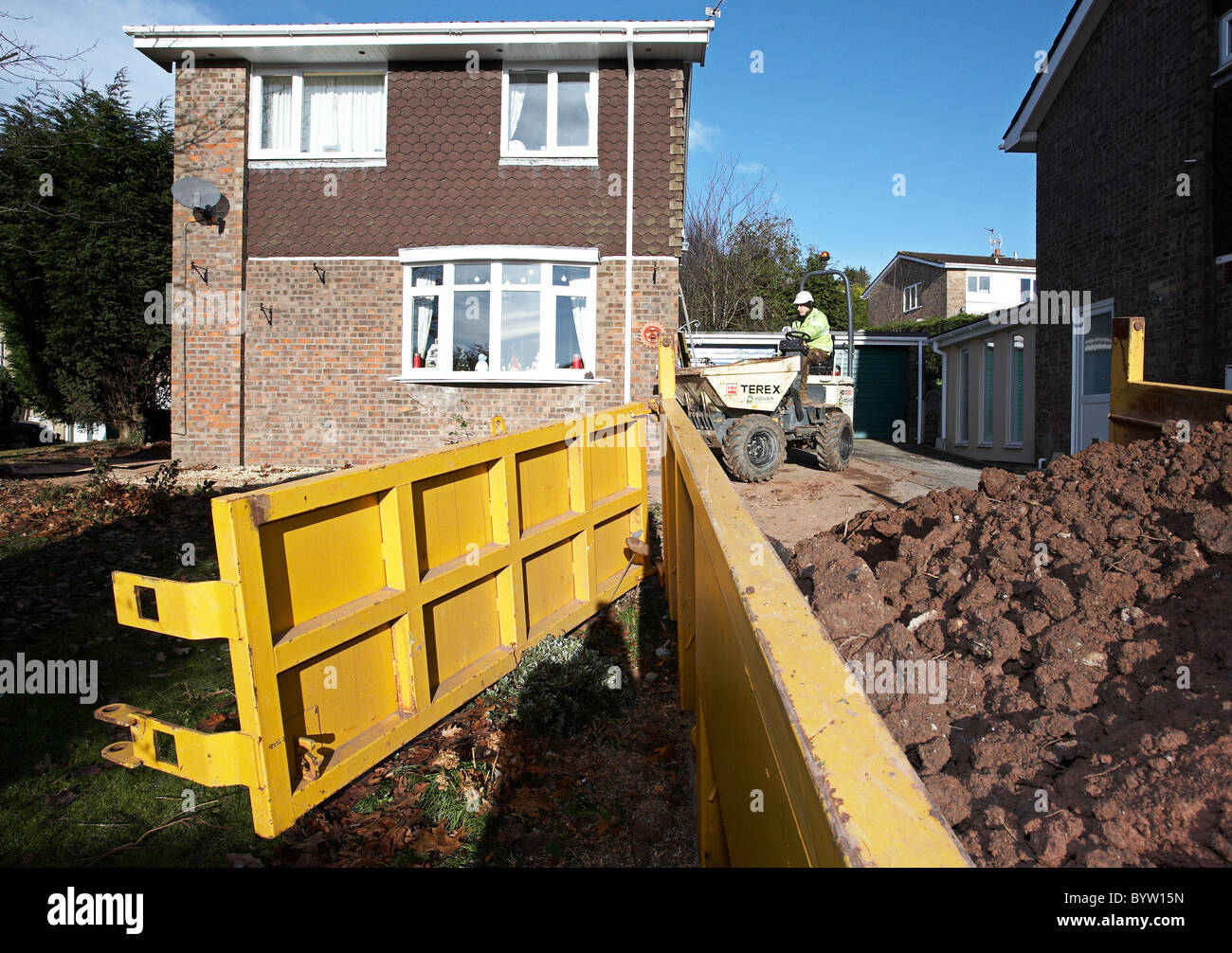 A skip being filled by a dump truck with earth outside a house Stock ...