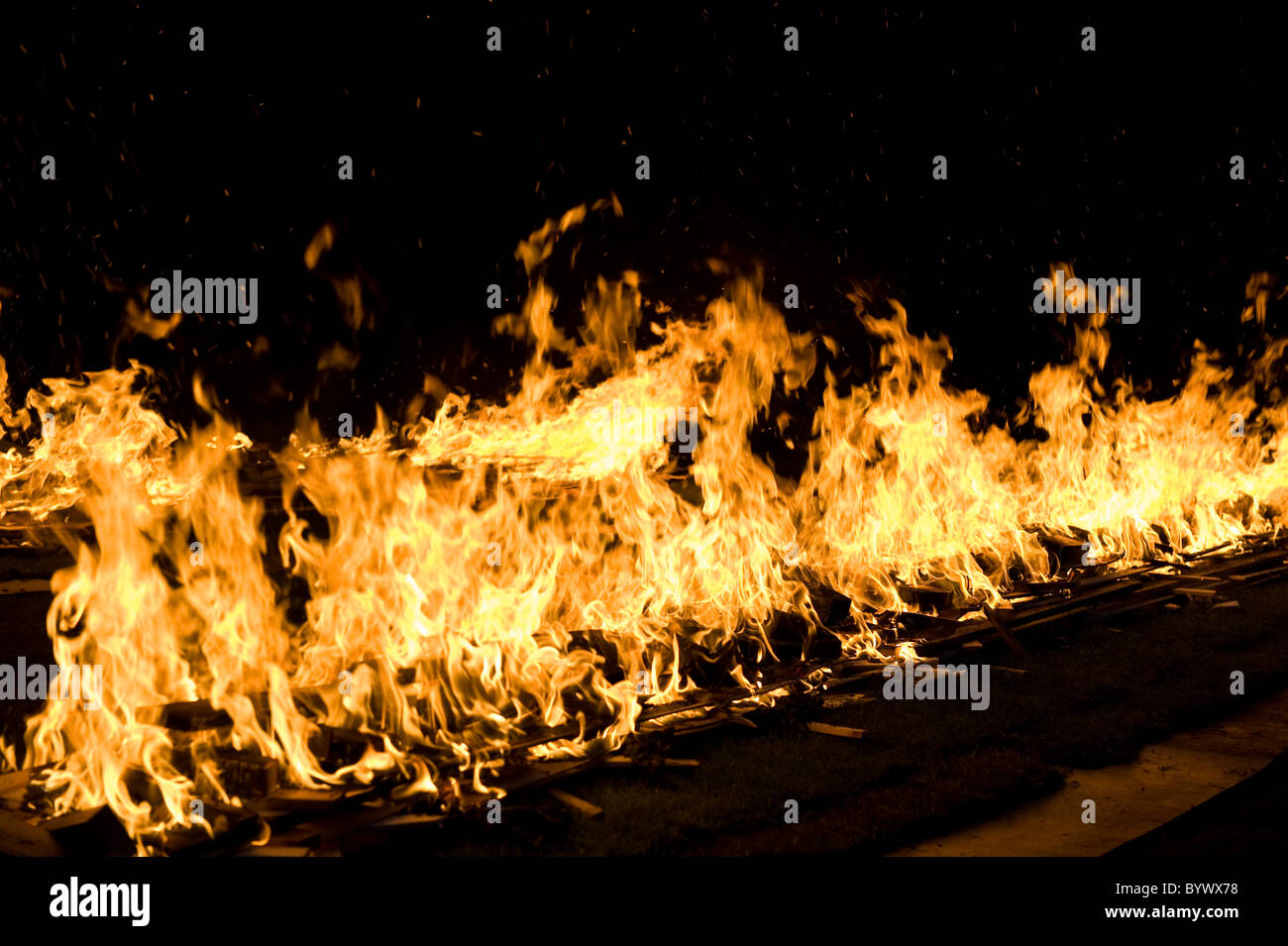 Flames rising from a firewalk in preparation using lines of wood logs ...