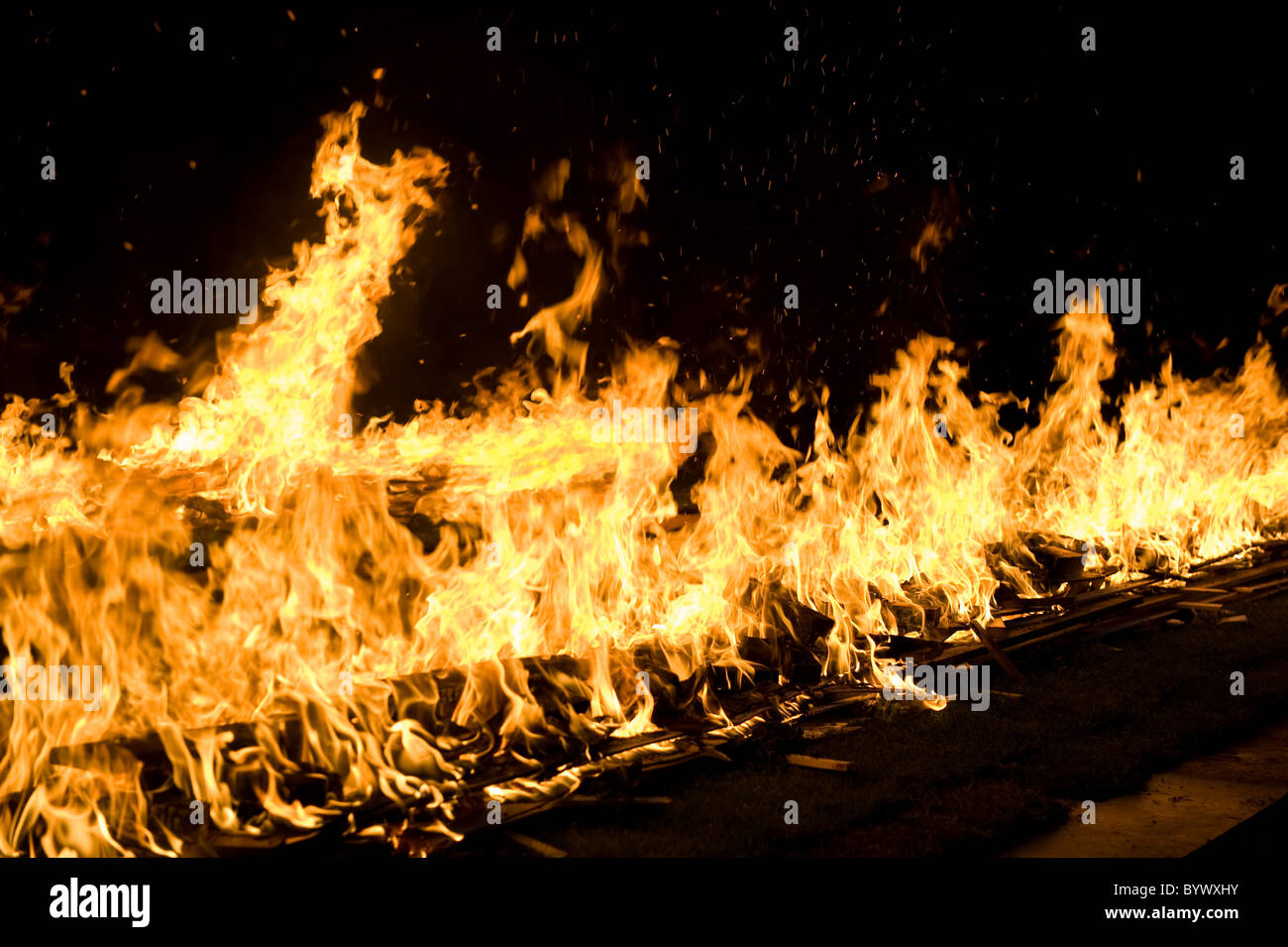 Flames rising from a firewalk in preparation using lines of wood logs ...