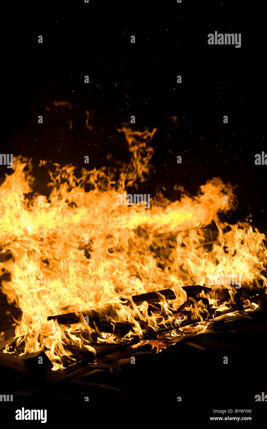 Flames rising from a firewalk in preparation using lines of wood logs ...