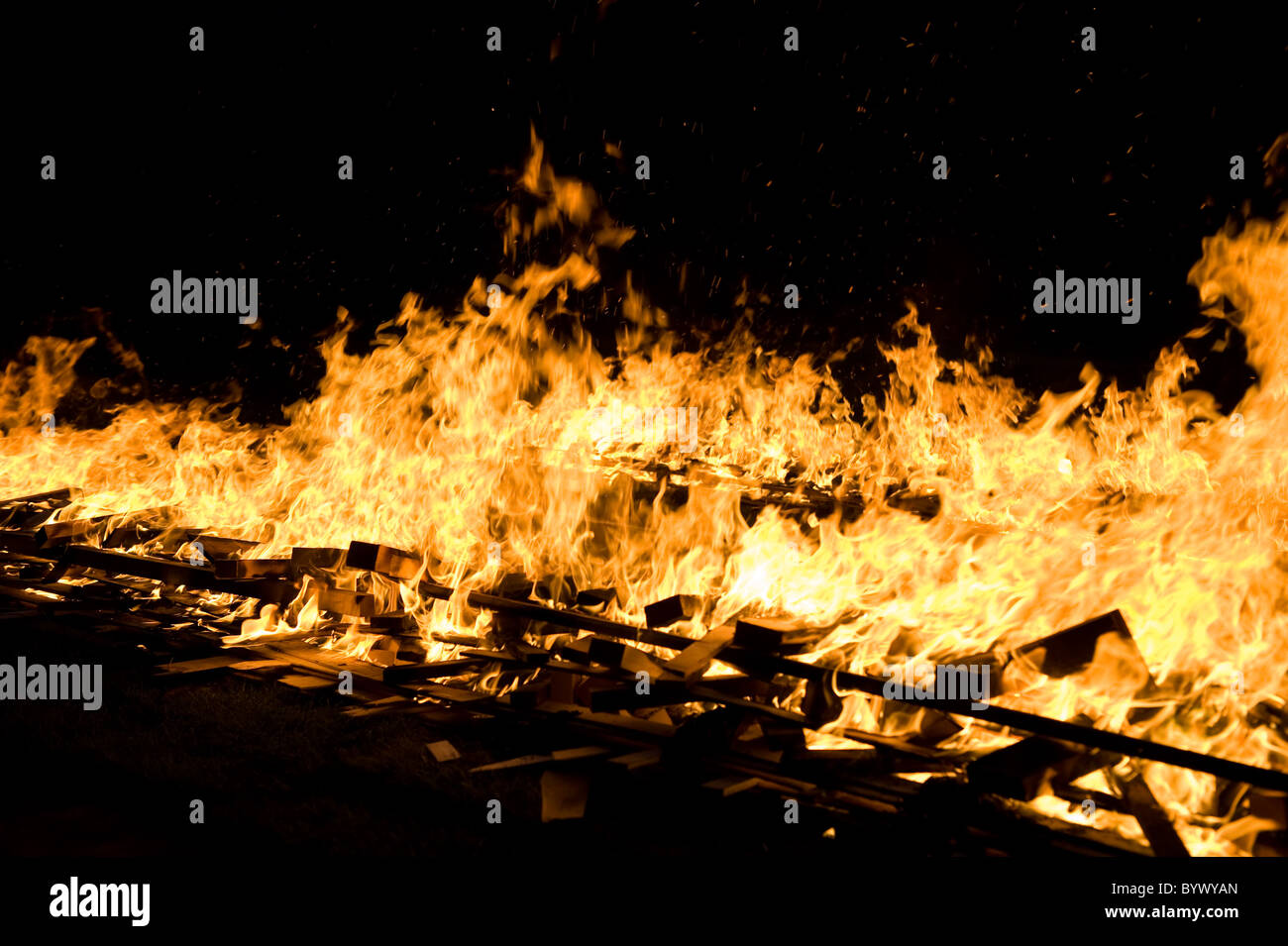 Flames rising from a firewalk in preparation using lines of wood logs ...