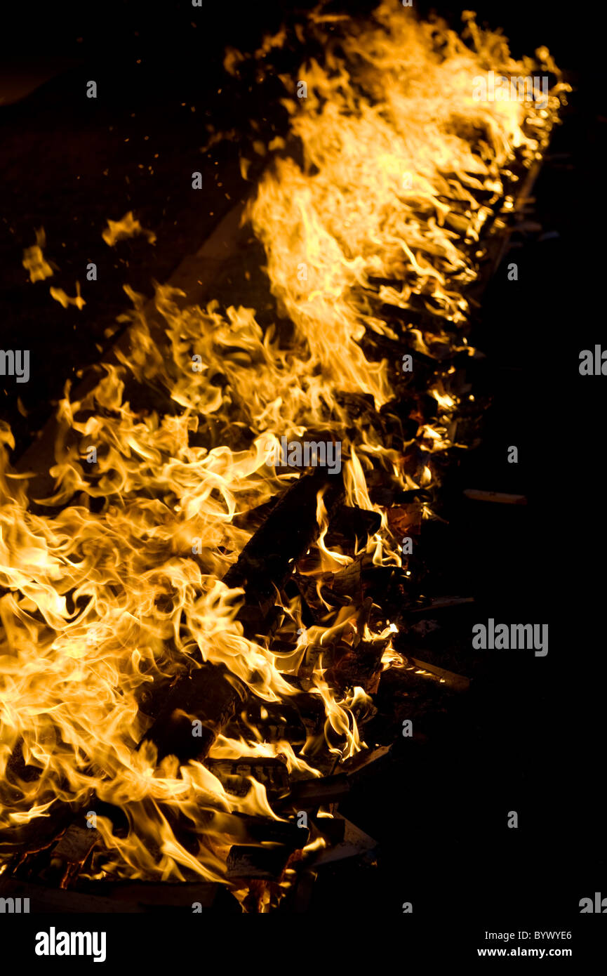 Flames rising from a firewalk in preparation using lines of wood logs ...