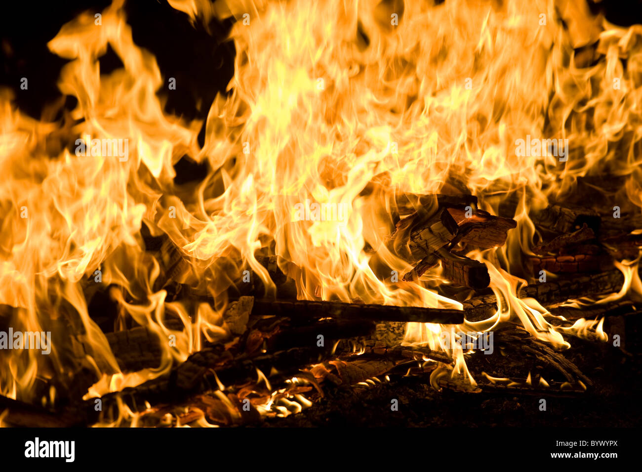 Flames rising from a firewalk in preparation using lines of wood logs ...