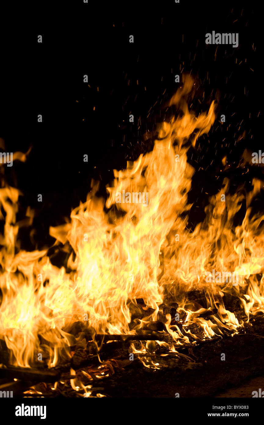 Flames rising from a firewalk in preparation using lines of wood logs ...