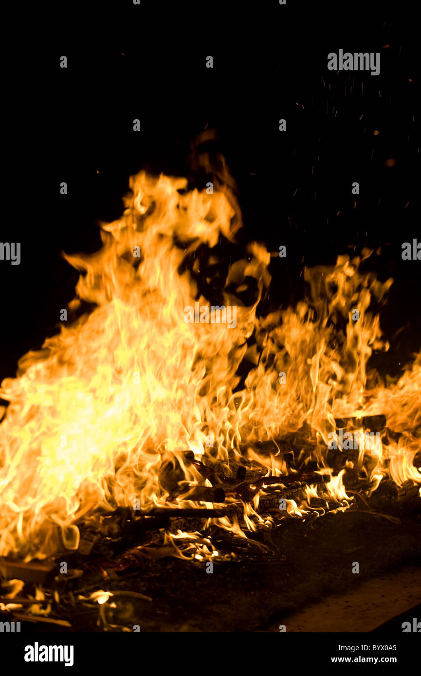 Flames rising from a firewalk in preparation using lines of wood logs ...