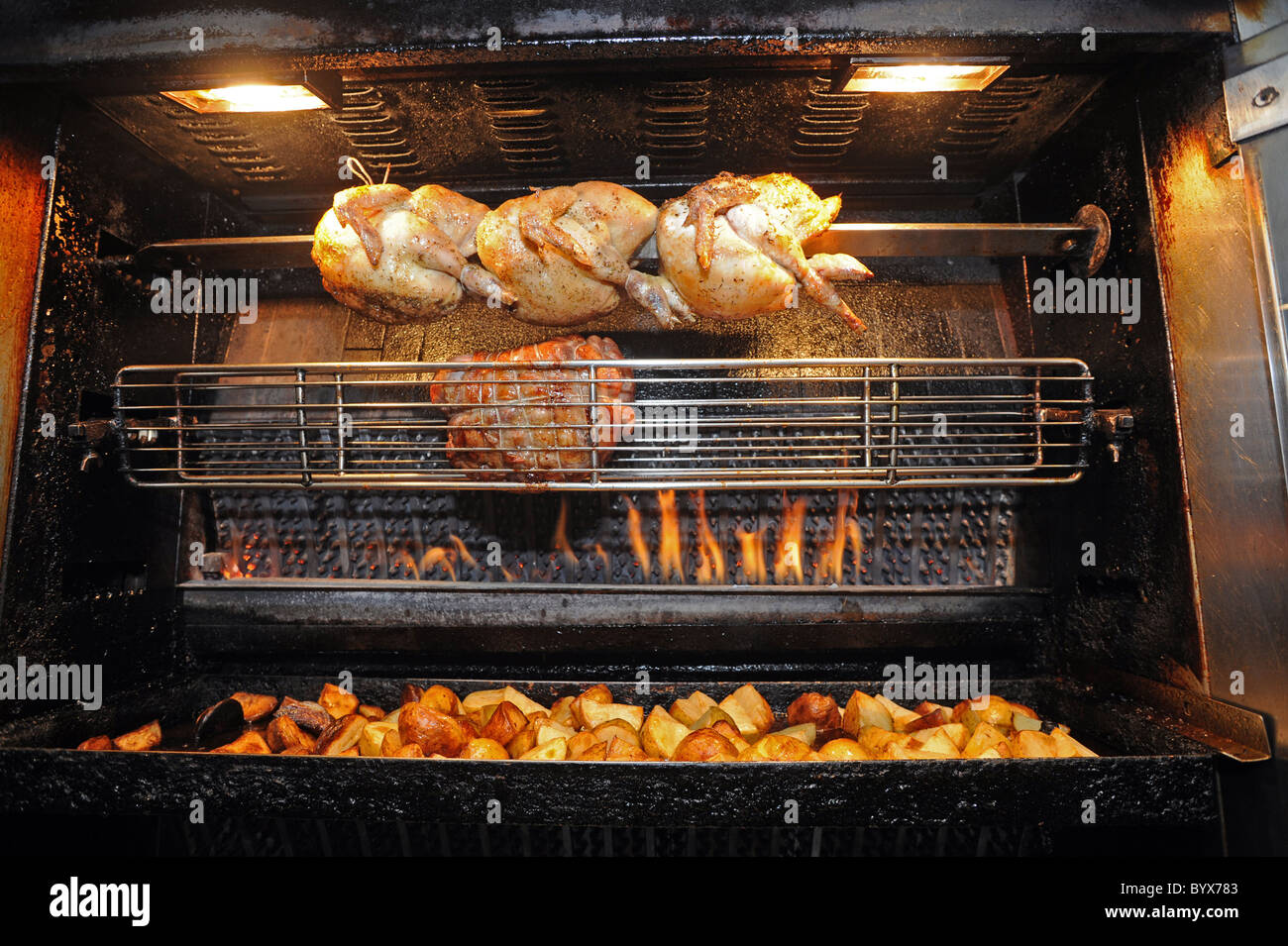 Chickens, Pork and potatoes roasting on a spit Stock Photo - Alamy