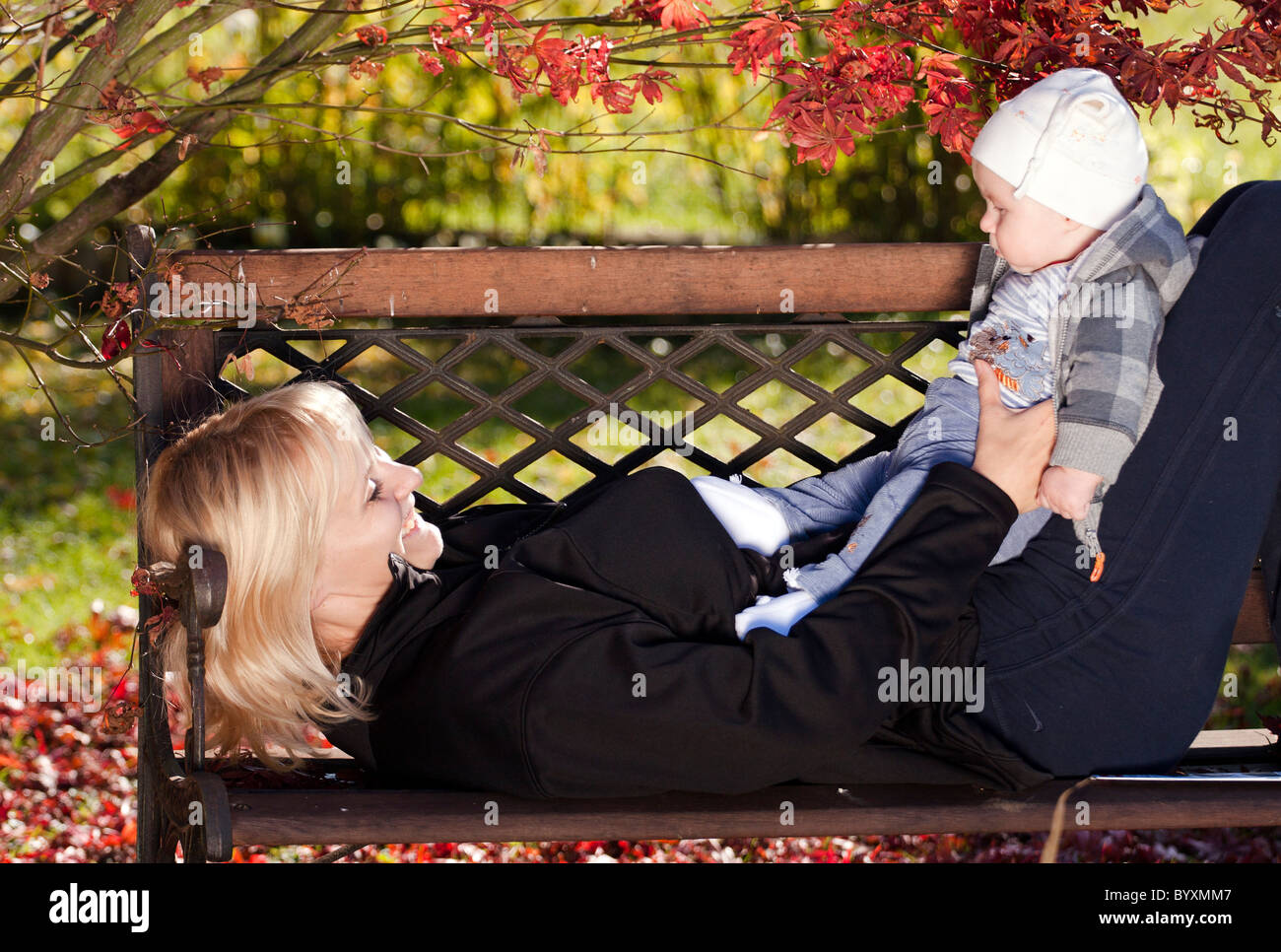 Motherlying on the bench with her baby in the autumn garden Stock Photo ...