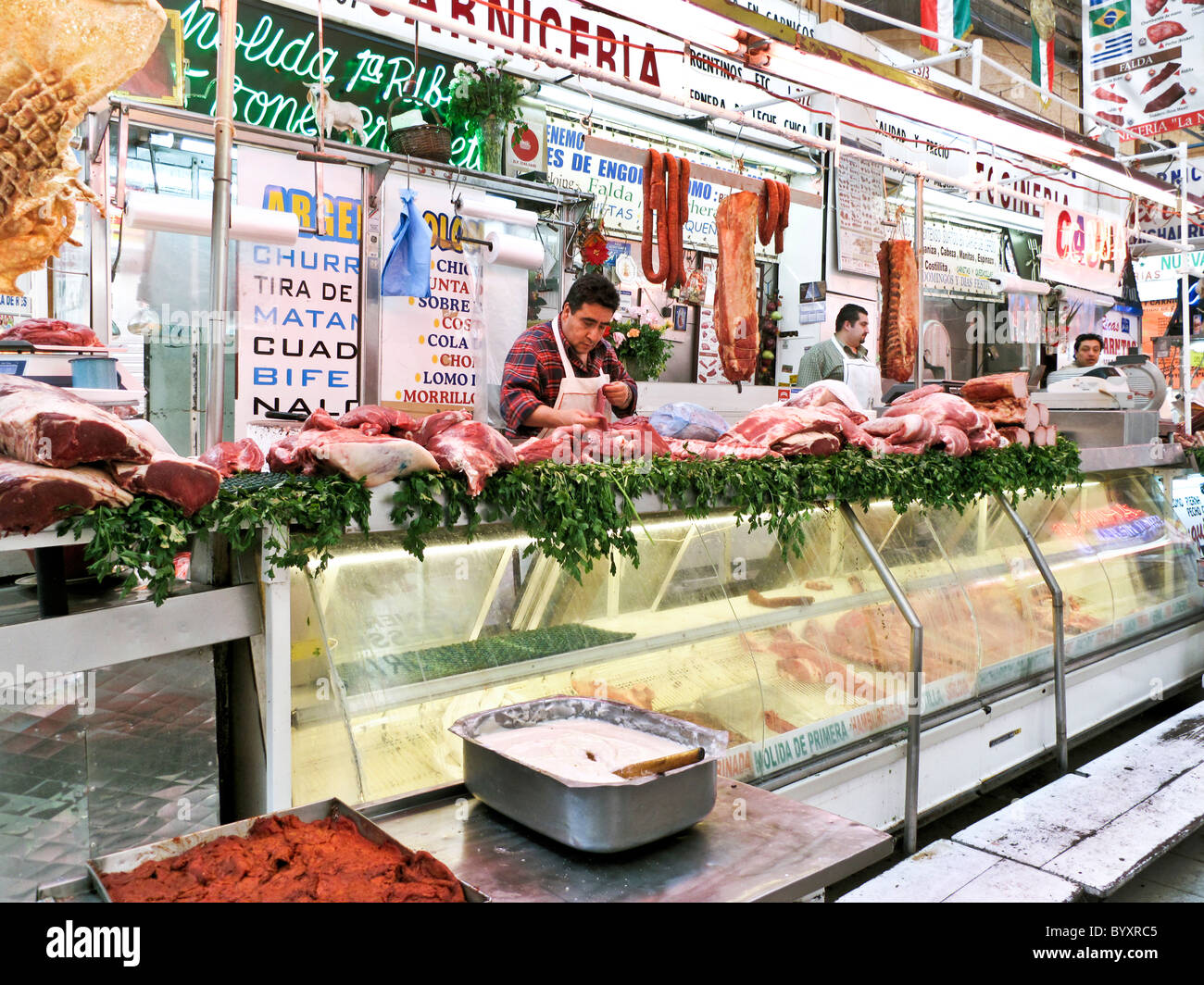 butchers working at brightly lit butcher stall with counter piled with ...