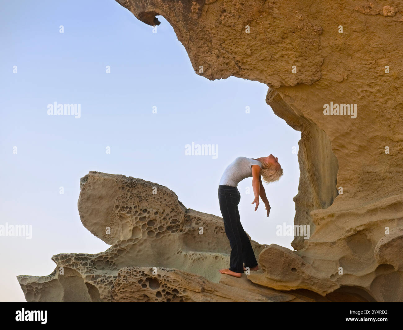 a woman bending backwards and looking up under a rock formation in ...