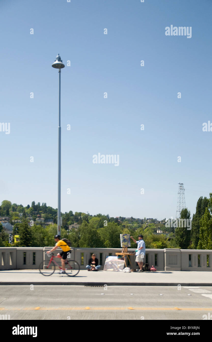 a sidewalk painter painting on canvas while a cyclist rides by; seattle ...