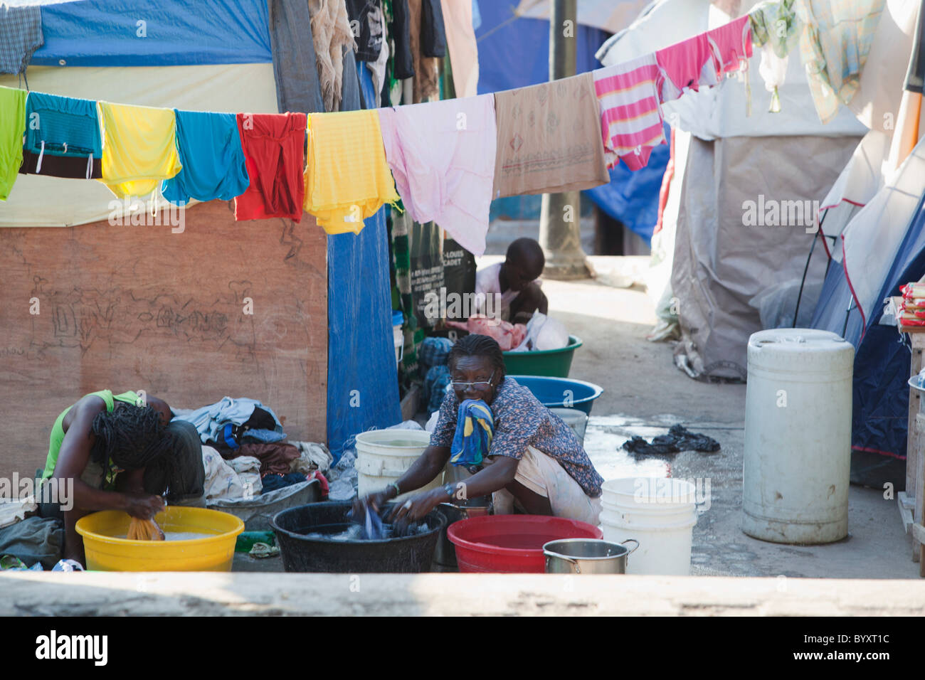 women wash clothes in large basins with a clothes line hanging above ...