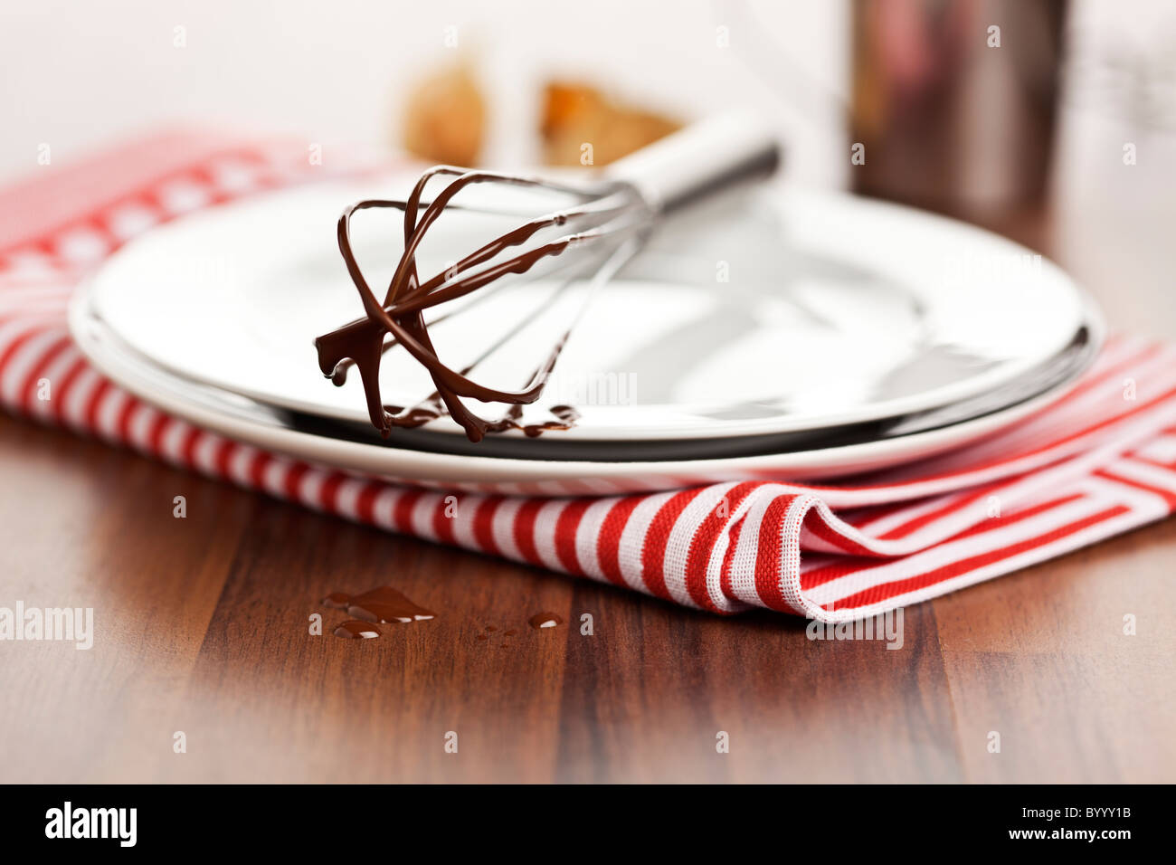 liquid chocolate dripping from a whisk laying on a plate, shallow depth ...