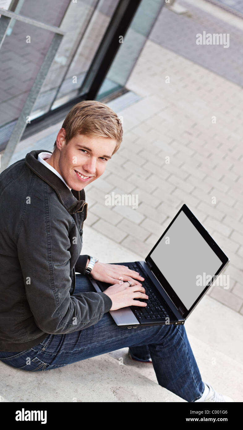 Young blond handsome smiling guy sitting outdoors with laptop computer ...
