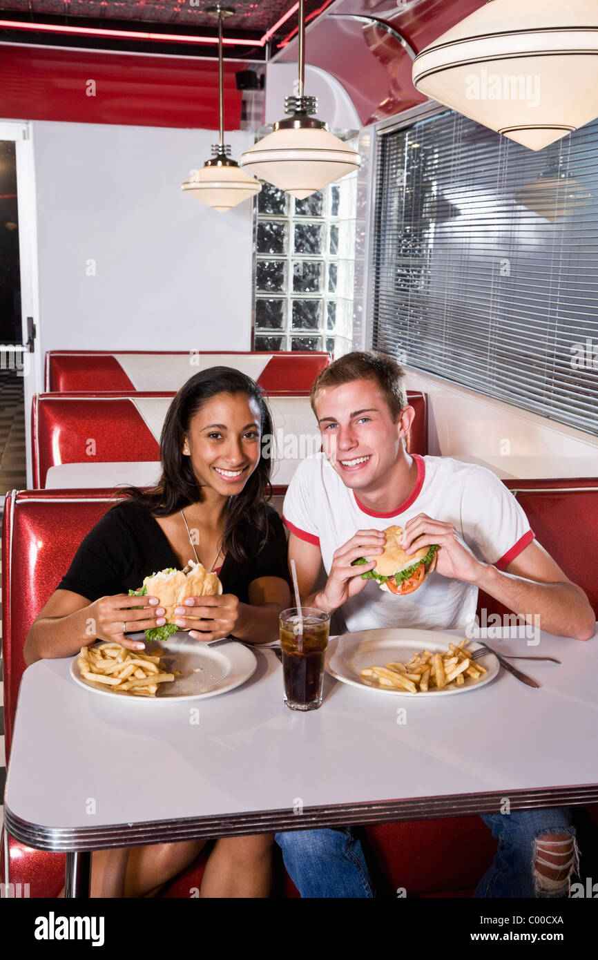 Interracial teen couple eating burgers in diner Stock Photo - Alamy