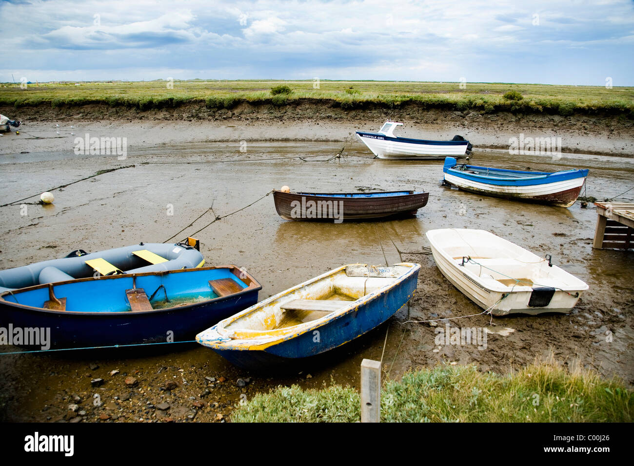 Boats in mud of small estuary by marshes Stock Photo - Alamy