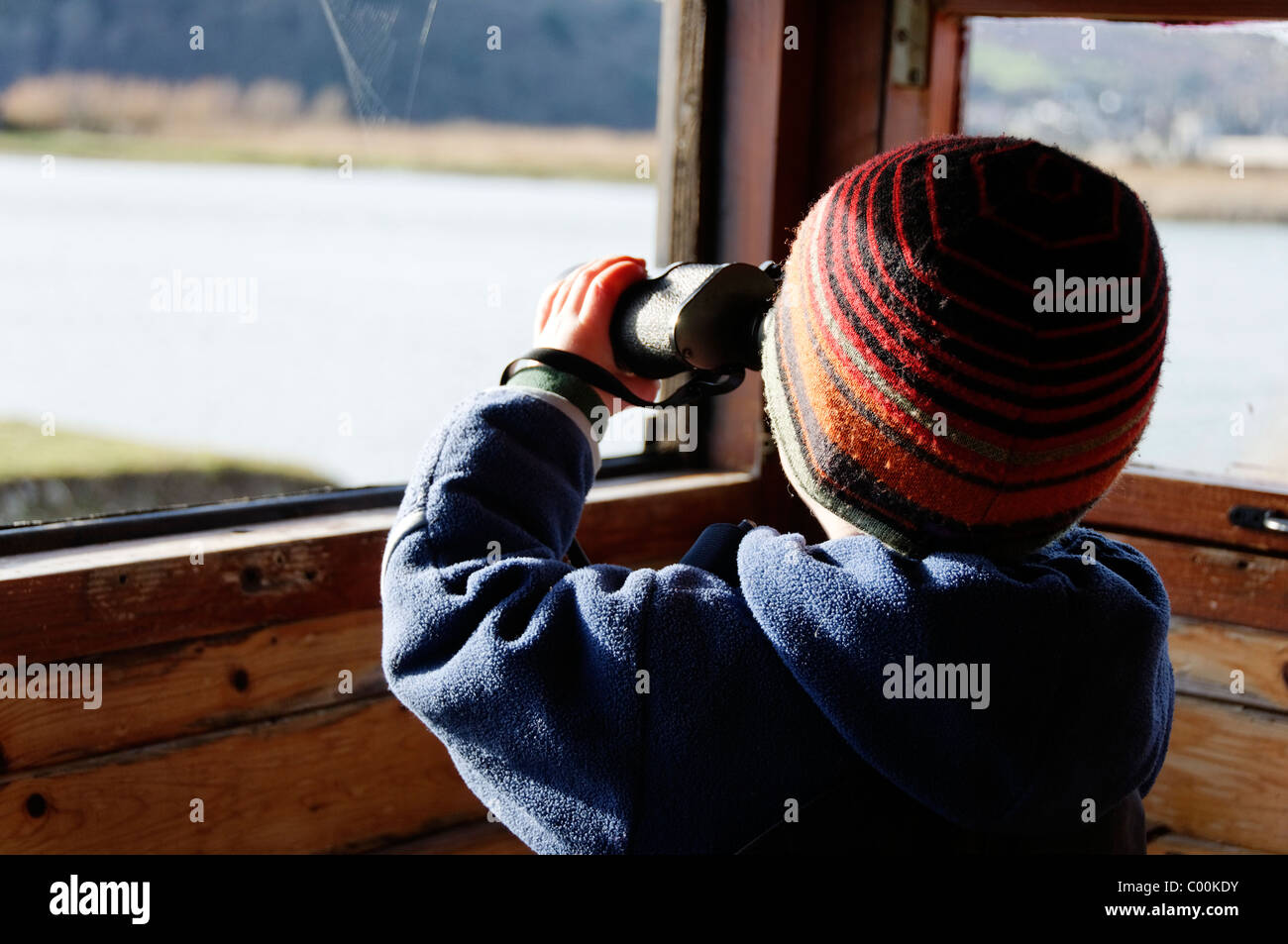 A young boy looking through binoculars from a bird hide at RSPB Conwy ...