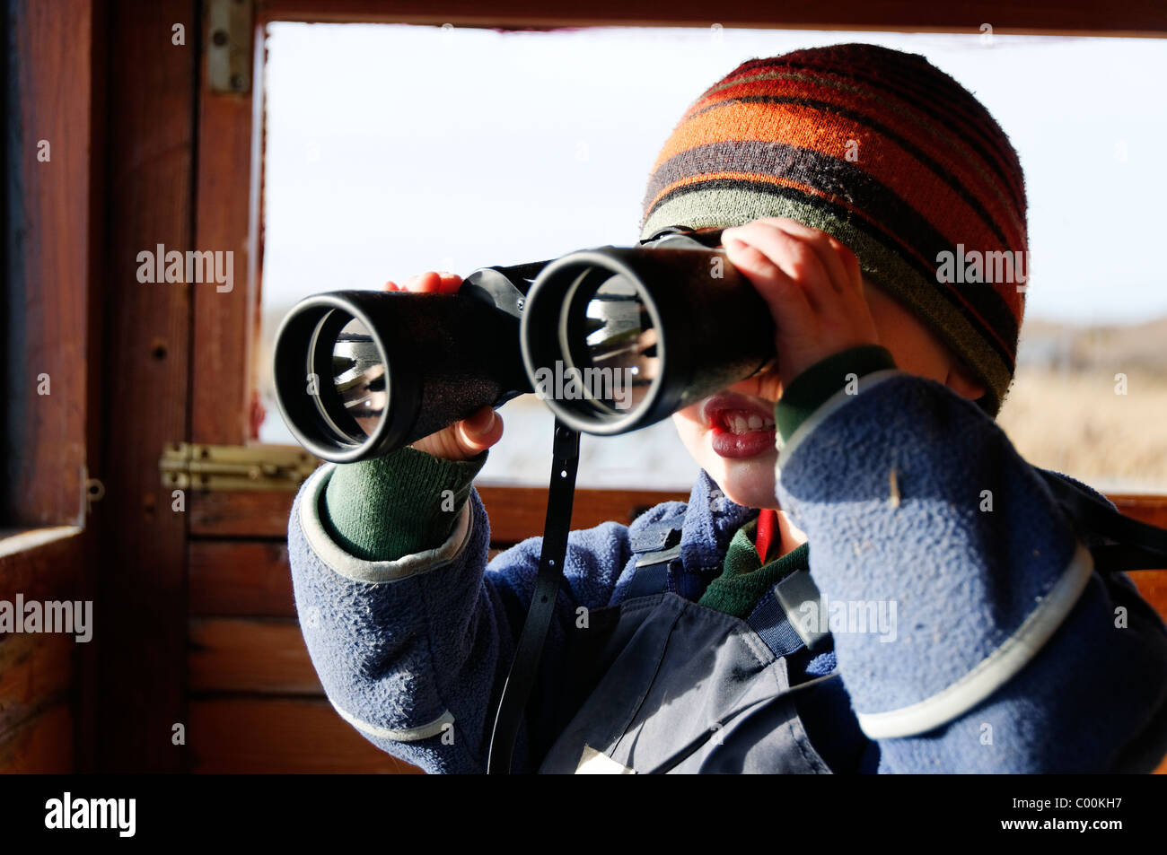 A young boy looking through binoculars from a bird hide at RSPB Conwy ...