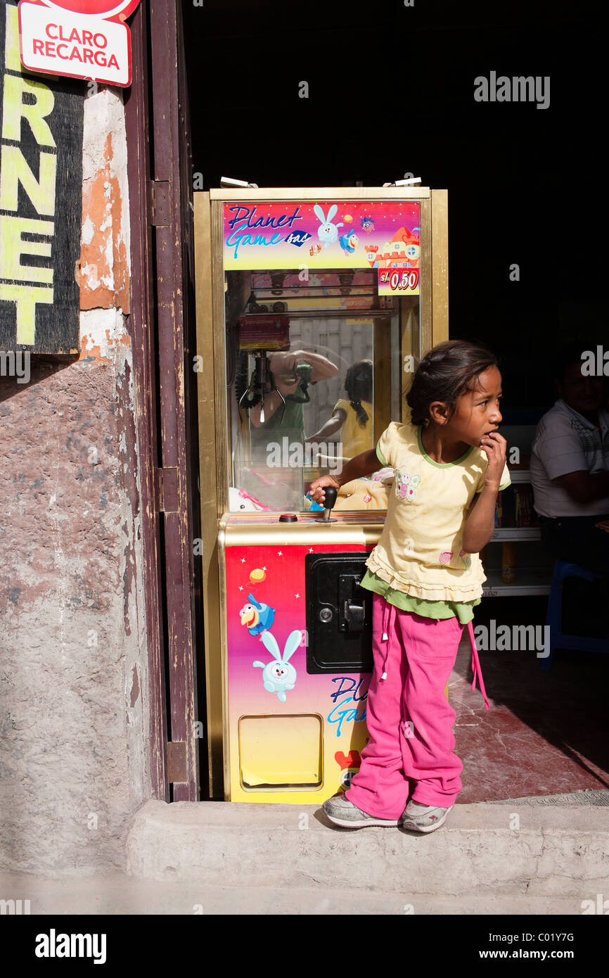 A young girl plays with a vending game machine on a street in Ayacucho ...