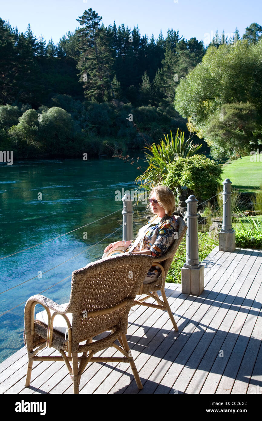 A woman sits in a deck chair viewing the blue waters of a river at ...