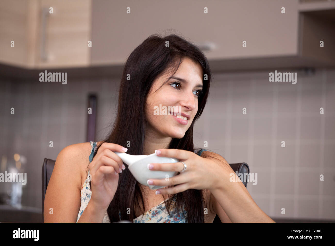 Young woman sitting at the dining table in the kitchen and eating Stock ...