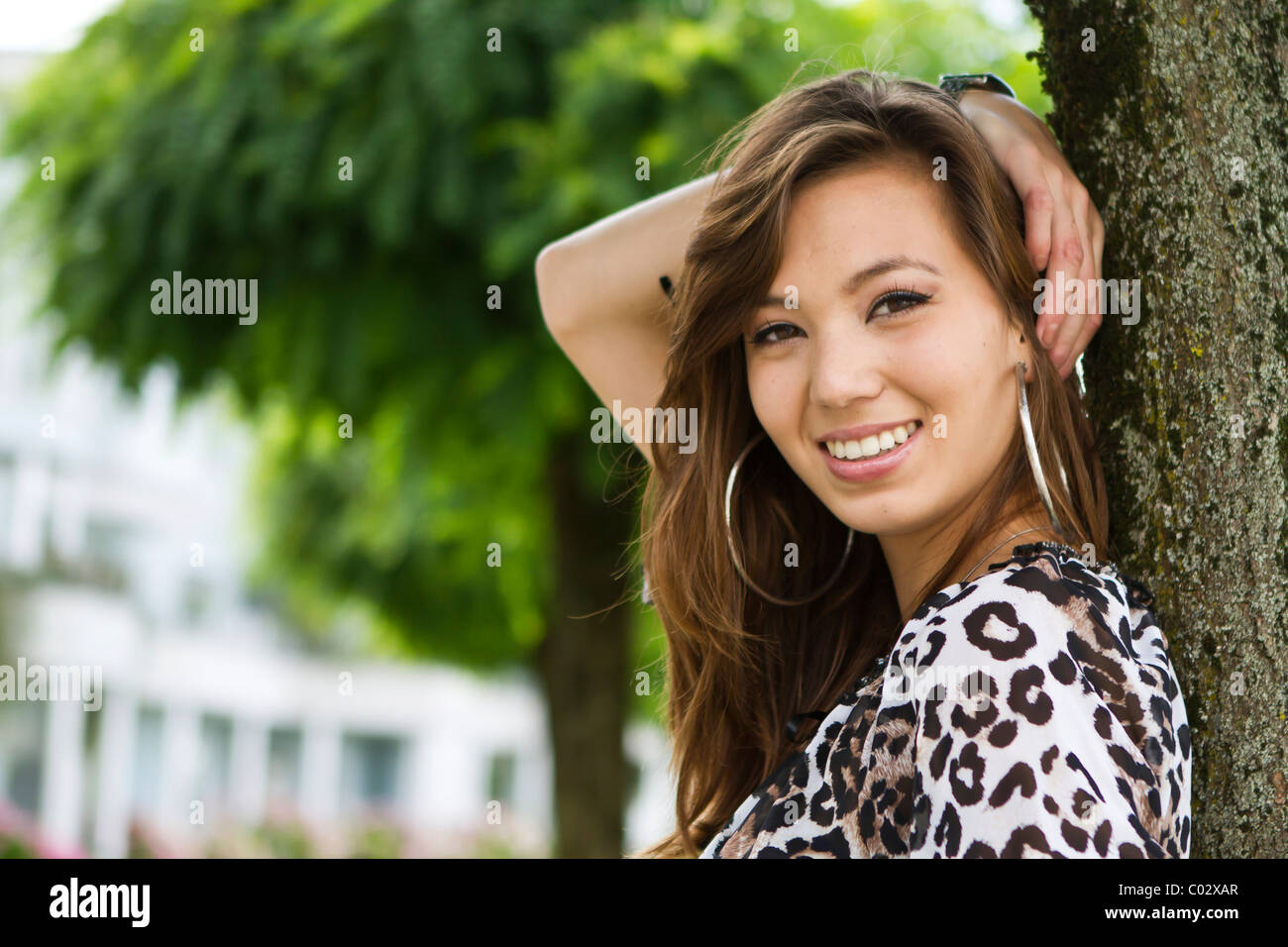 Young woman wearing leopard-print top leaning against tree Stock Photo ...