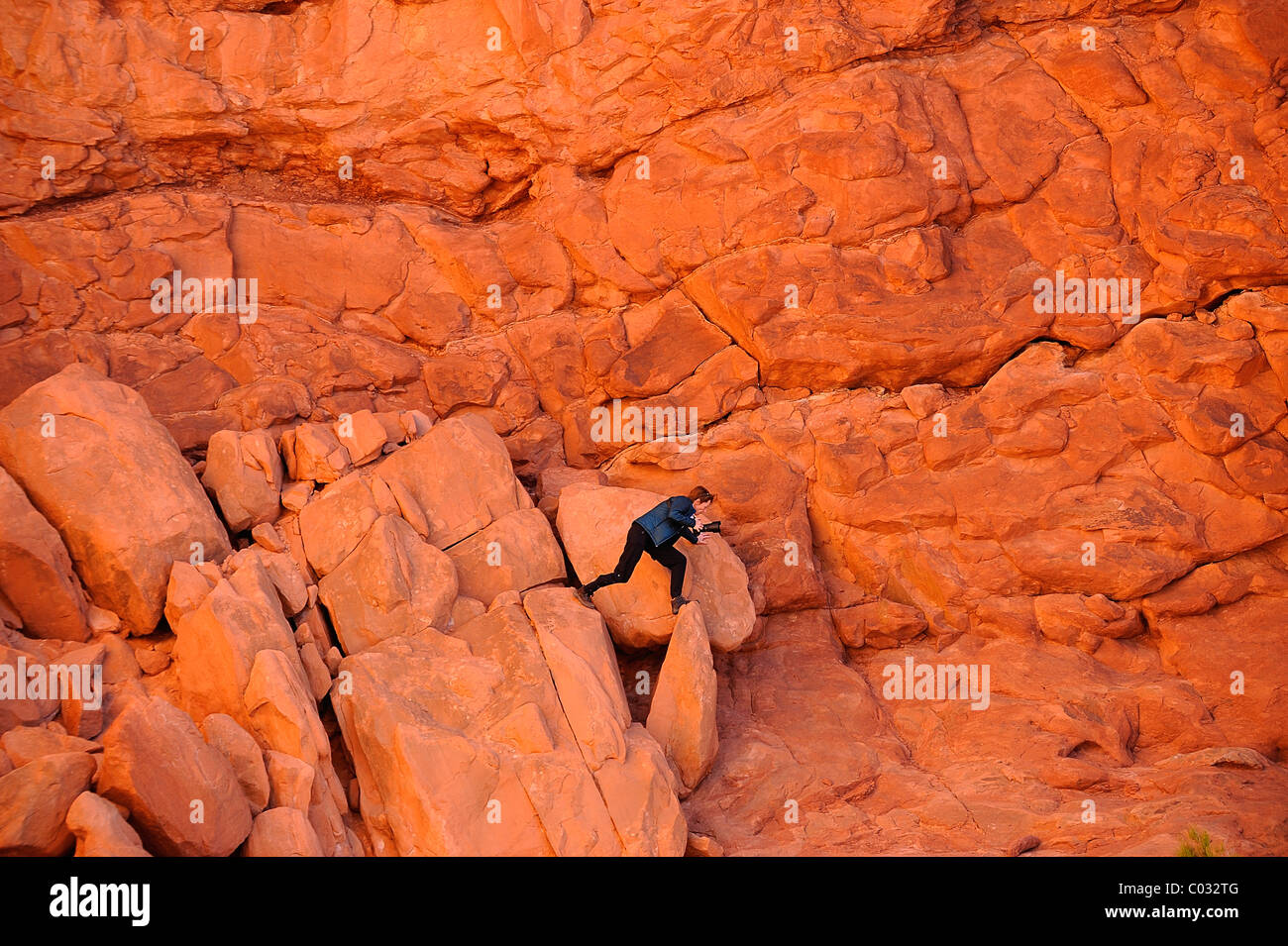 Woman photographer climbing rocks, carrying a SLR camera in Canyonlands ...