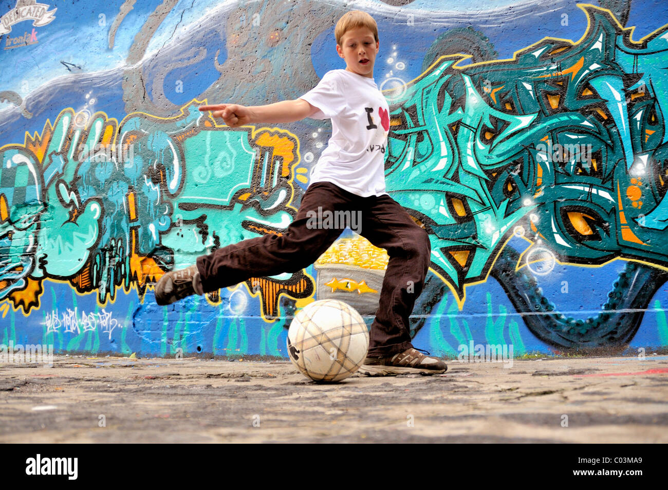 Boy, 10, playing football in front of a wall with graffiti, Germany ...