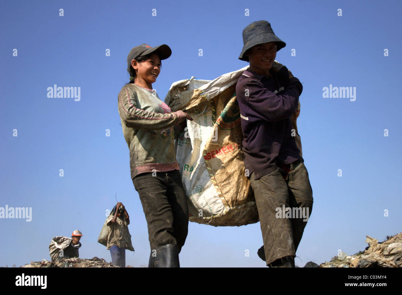 A young man and woman are carrying a large bag filled with garbage at a ...