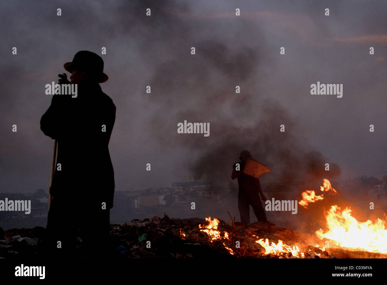 A worker shields his face from burning garbage as another man looks ...