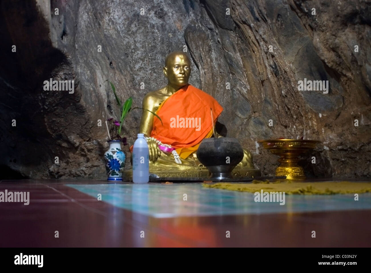 A Buddha statue of a monk with an orange robe is displayed in an ...