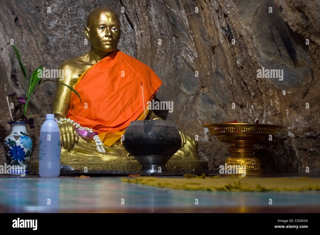A Buddha statue of a monk with an orange robe is displayed in an ...