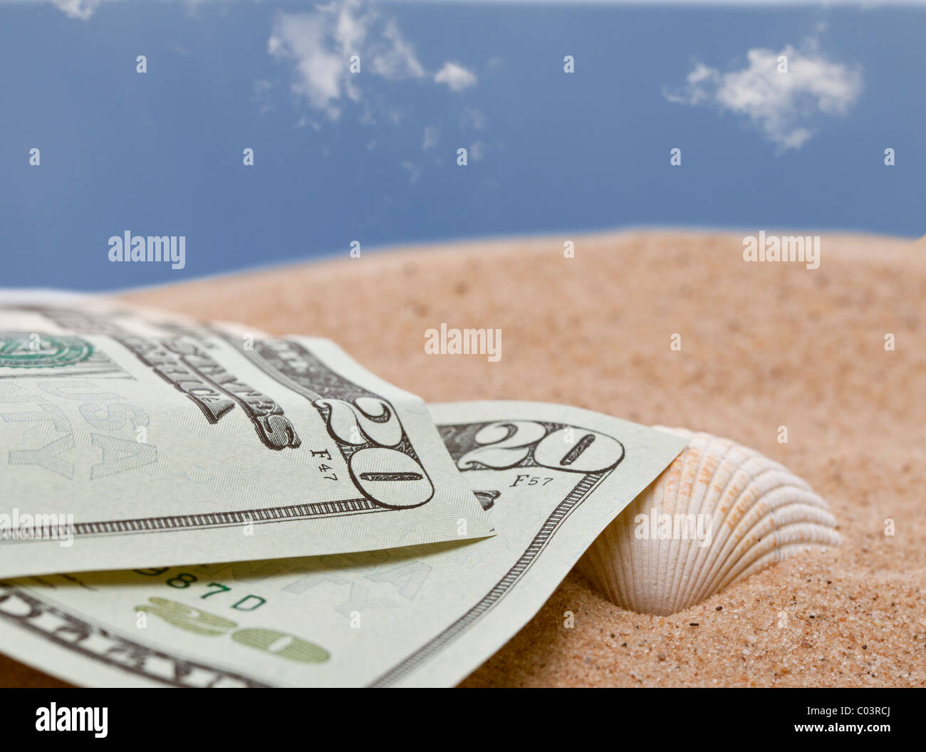 Two twenty dollar notes and a seashell on a beach with a blue sky with ...