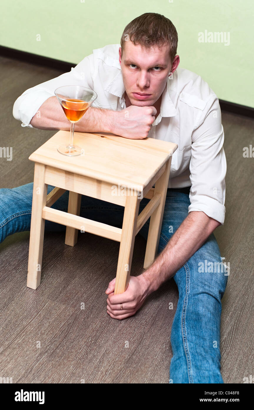 Drunken man sitting on floor with glass of alcohol and holding stool ...