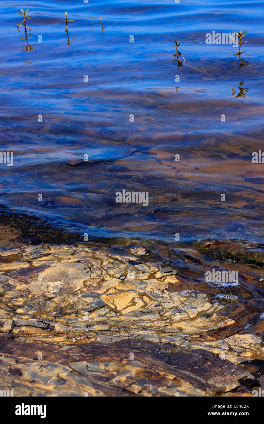 Reflections of the sky in the water lapping rocks at lake's edge Stock ...