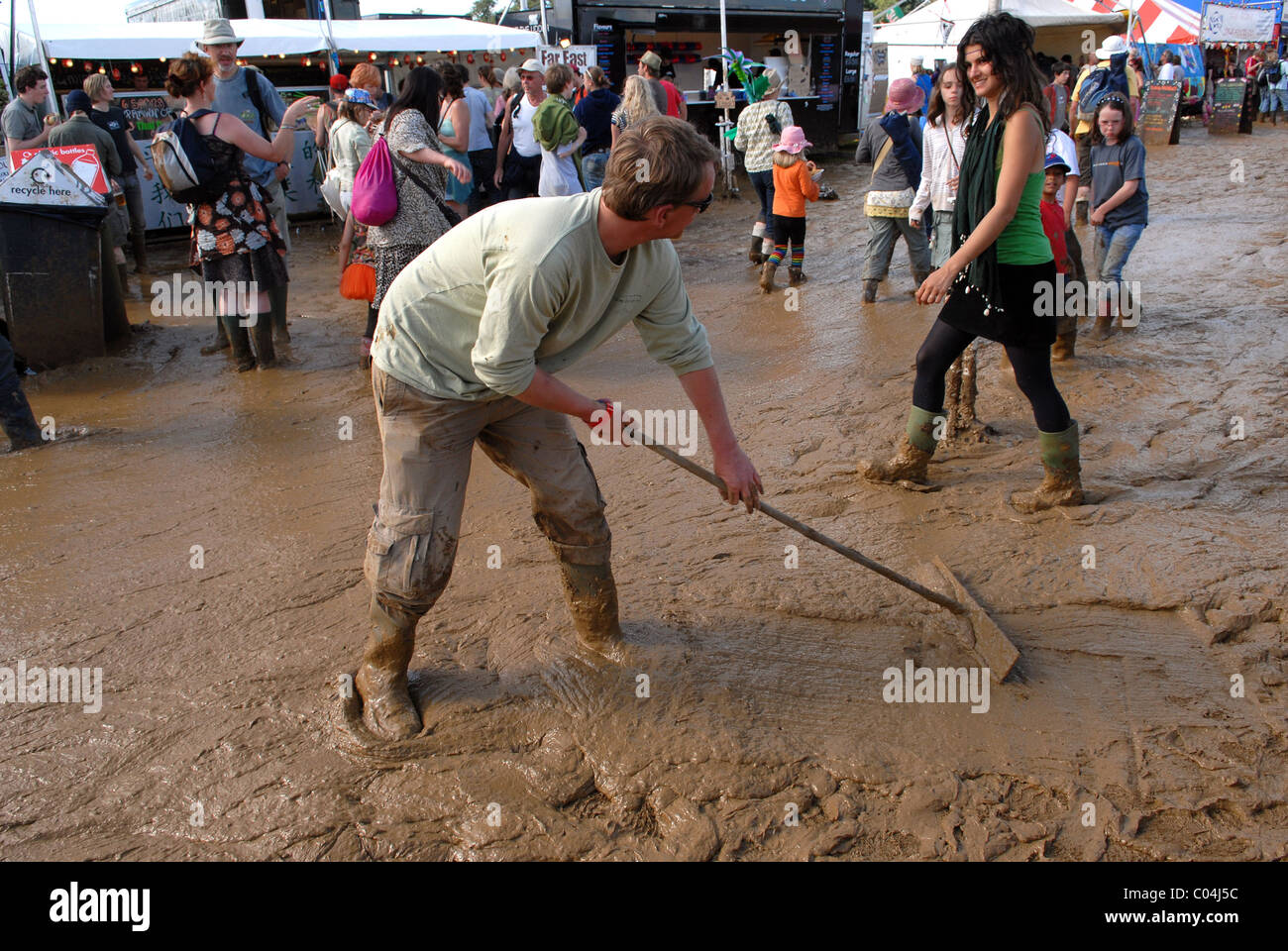 Young man raking sloppy mud from paths at WOMAD Festival, Malmesbury ...