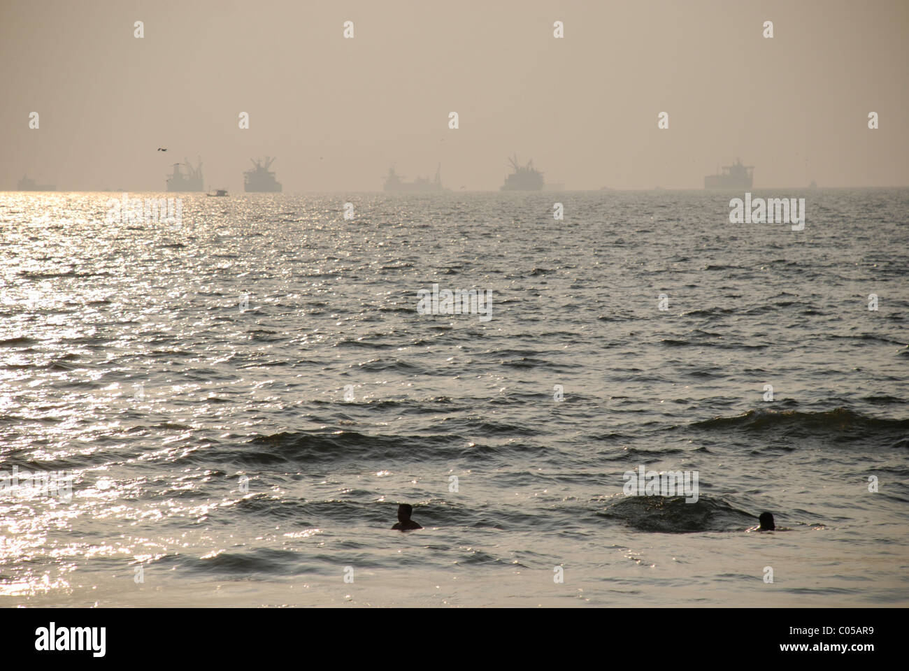 Off a beach in Goa, two men swim before a backdrop of cargo ships Stock ...