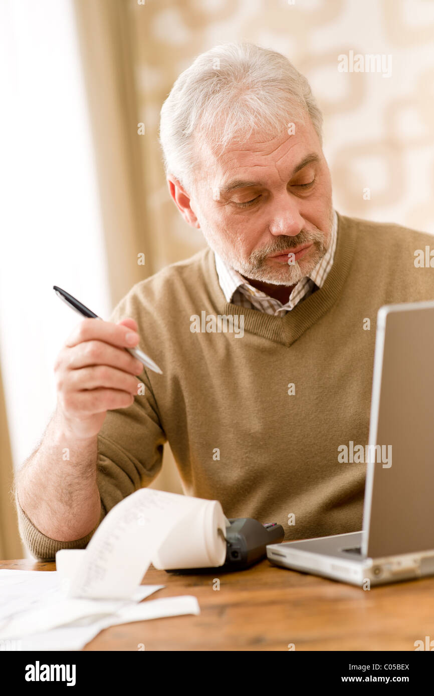 Senior mature man - home office using paper tape calculator and laptop ...