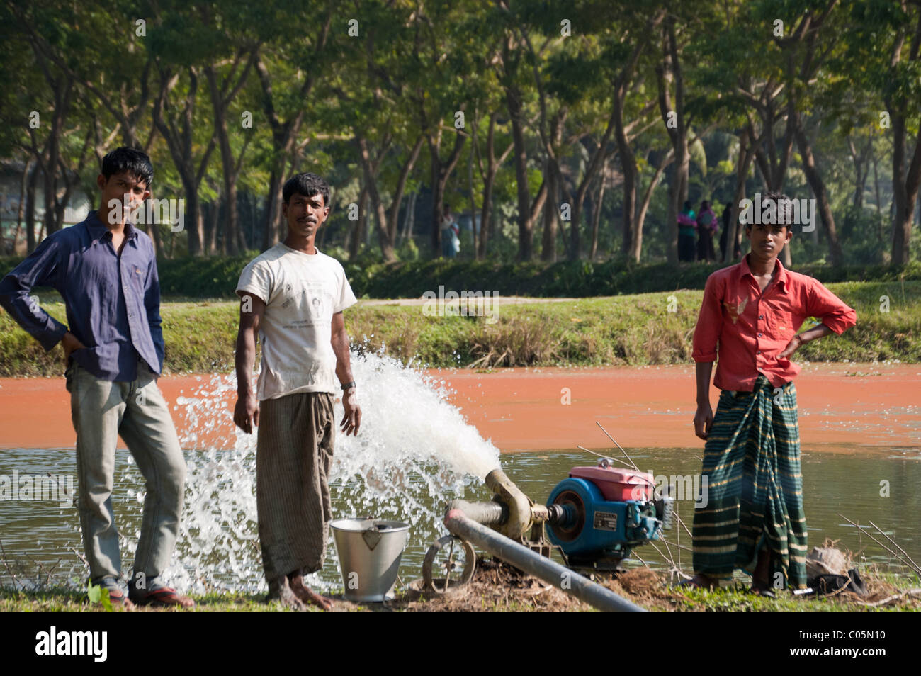 Three Bangladeshi men operating a water pump, which is pumping water ...
