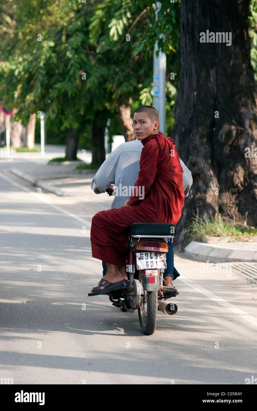 Buddhist Monk riding on the back of a motorbike on a street of Phnom ...